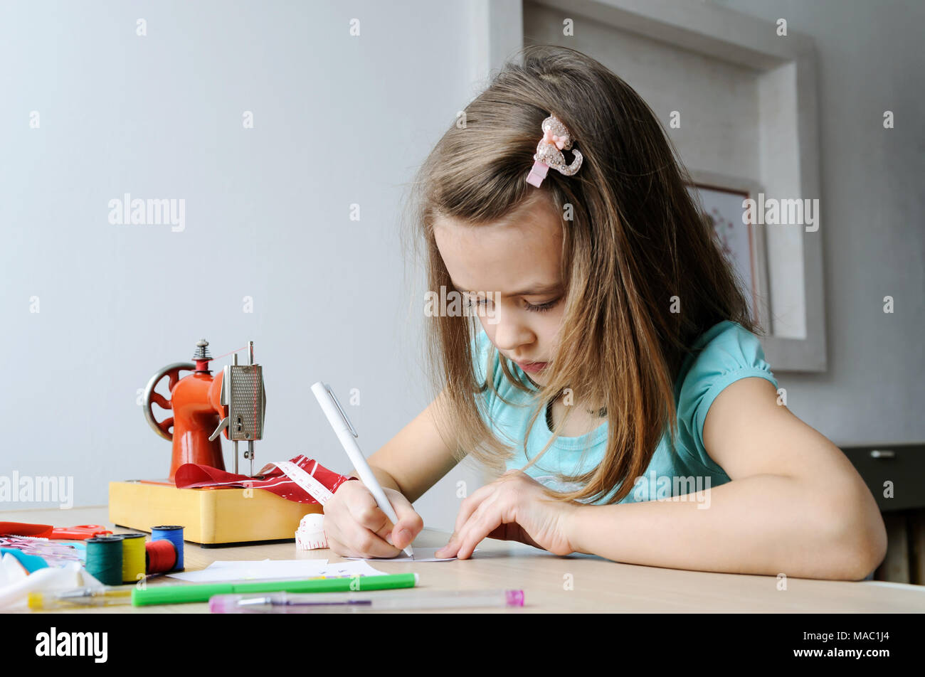 The girl is drawing a sketch of a dress for a doll. To sew it on a ...