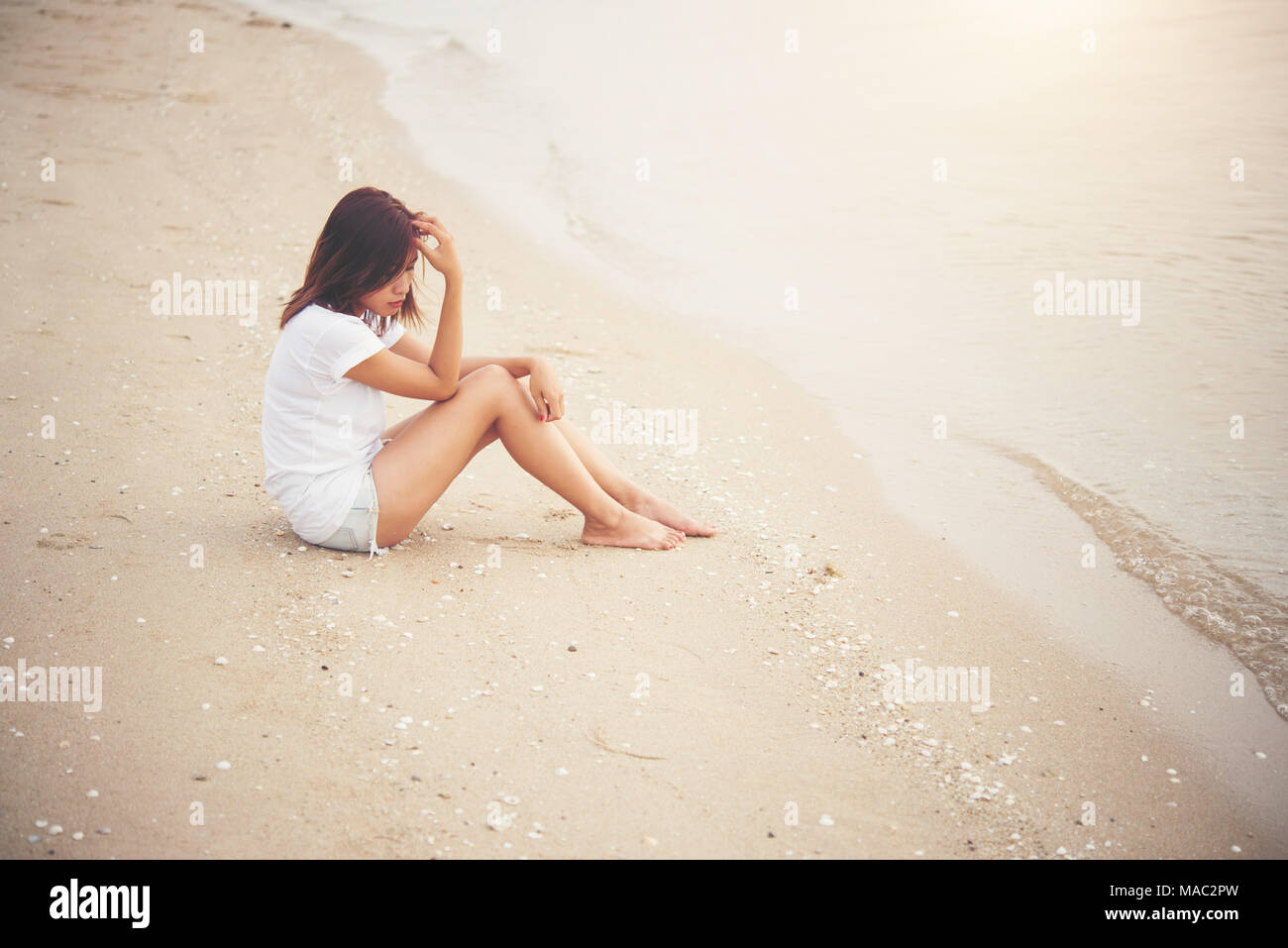 Young woman with looks lonely feel sit on the beach. Sad woman alone ...