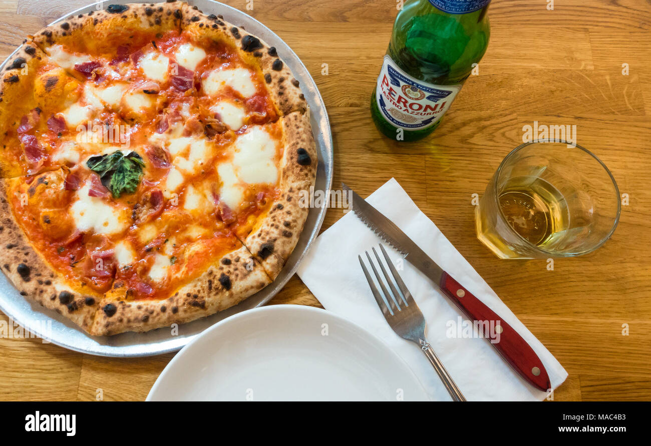 Pizza with mozzarella, tomatoes, cooked ham, and basil, with a Peroni ...