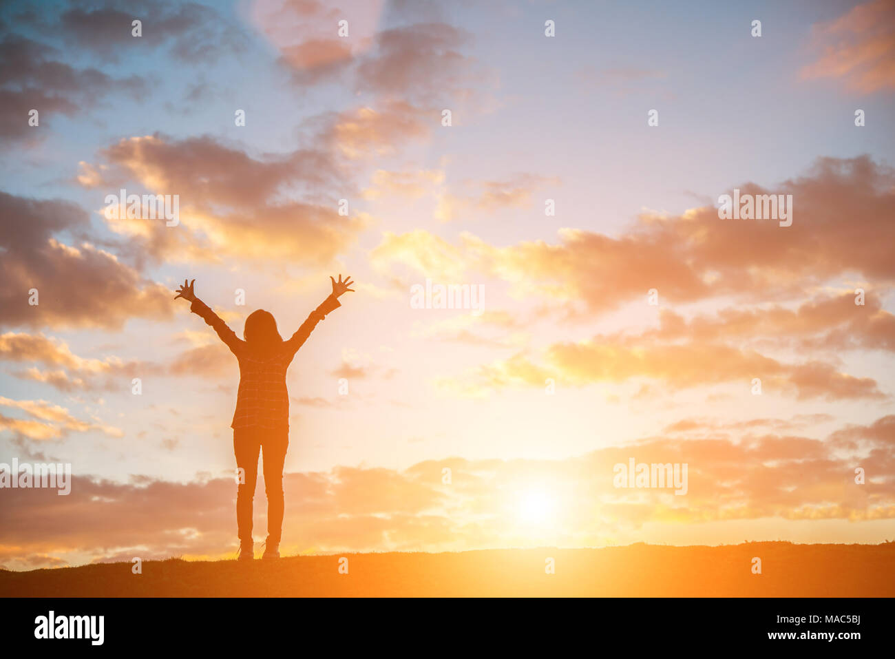 Silhouette woman at sunset standing elated with arms raised up above ...