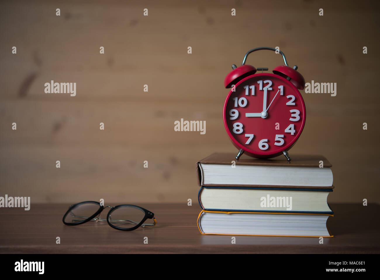 Alarm clock at 9am on stack of books with glasses on wooden table ...