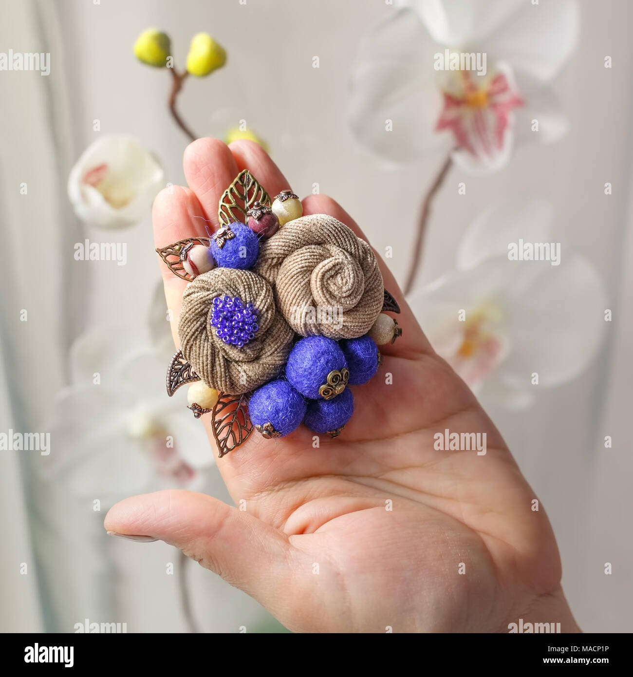 Small handmade brooch in the form of two beige flowers lies on the palm ...