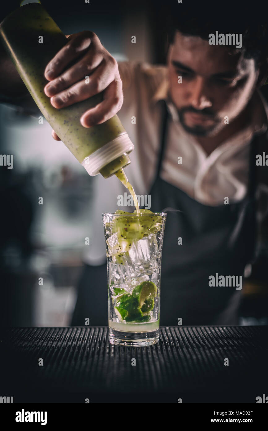 Barman pouring sweet syrup into the fresh sour lime and kiwi cocktail ...