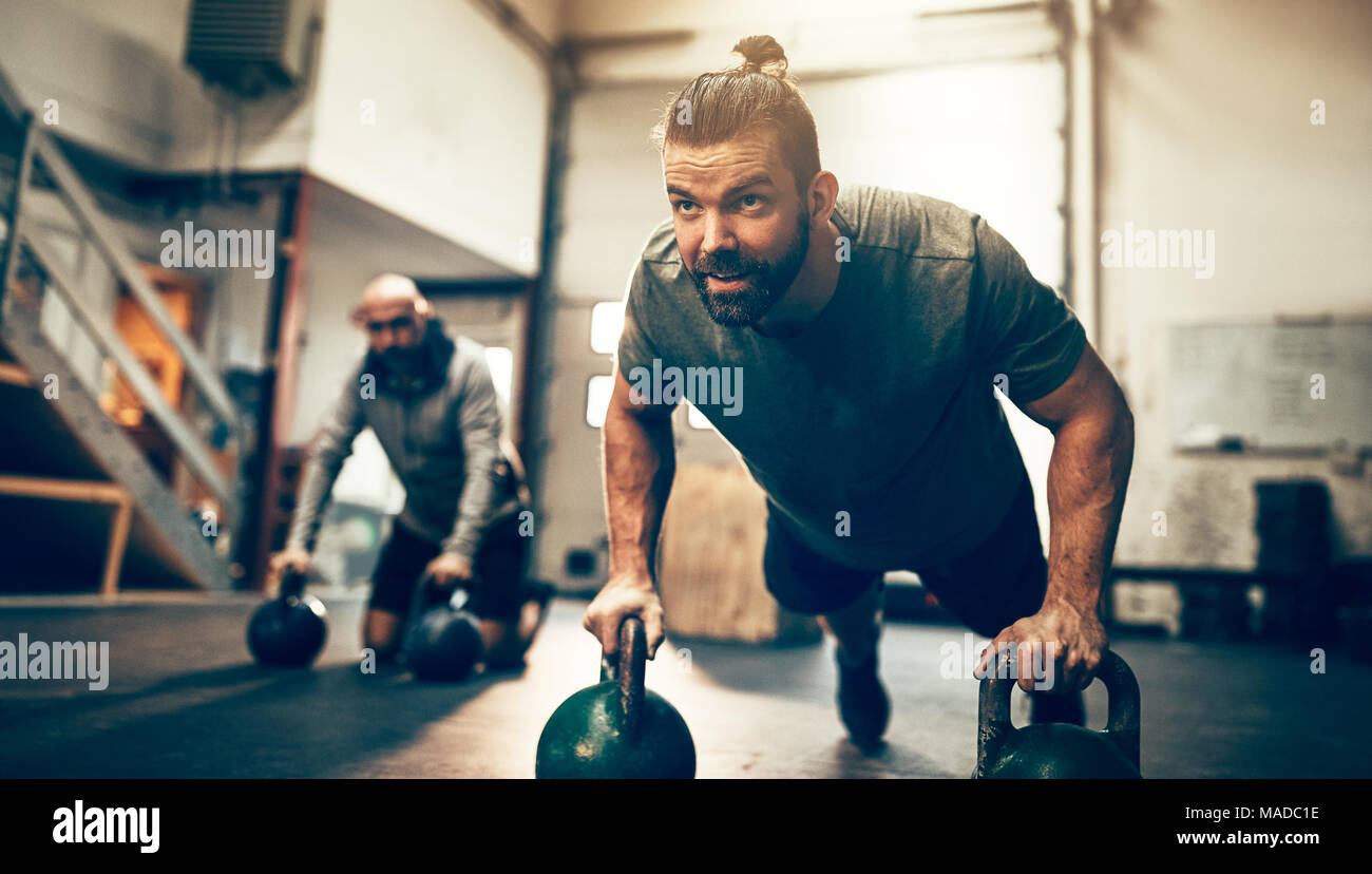 Fit young man doing pushups on dumbbells while working out during an ...
