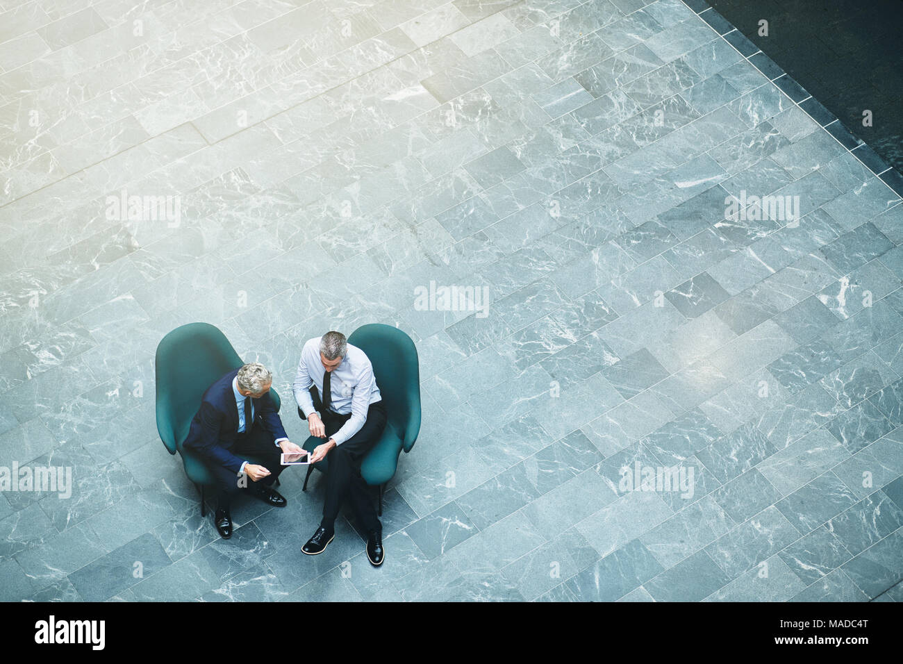 High angle of two mature businessmen talking together and using a digital tablet while sitting ...