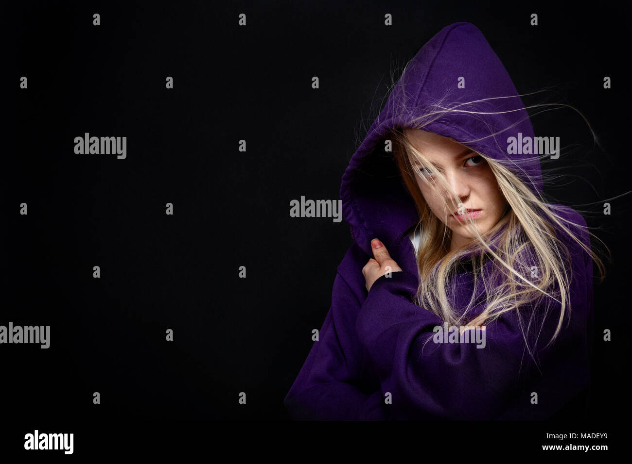 scared blonde girl with flying hairs in hood on black background with ...