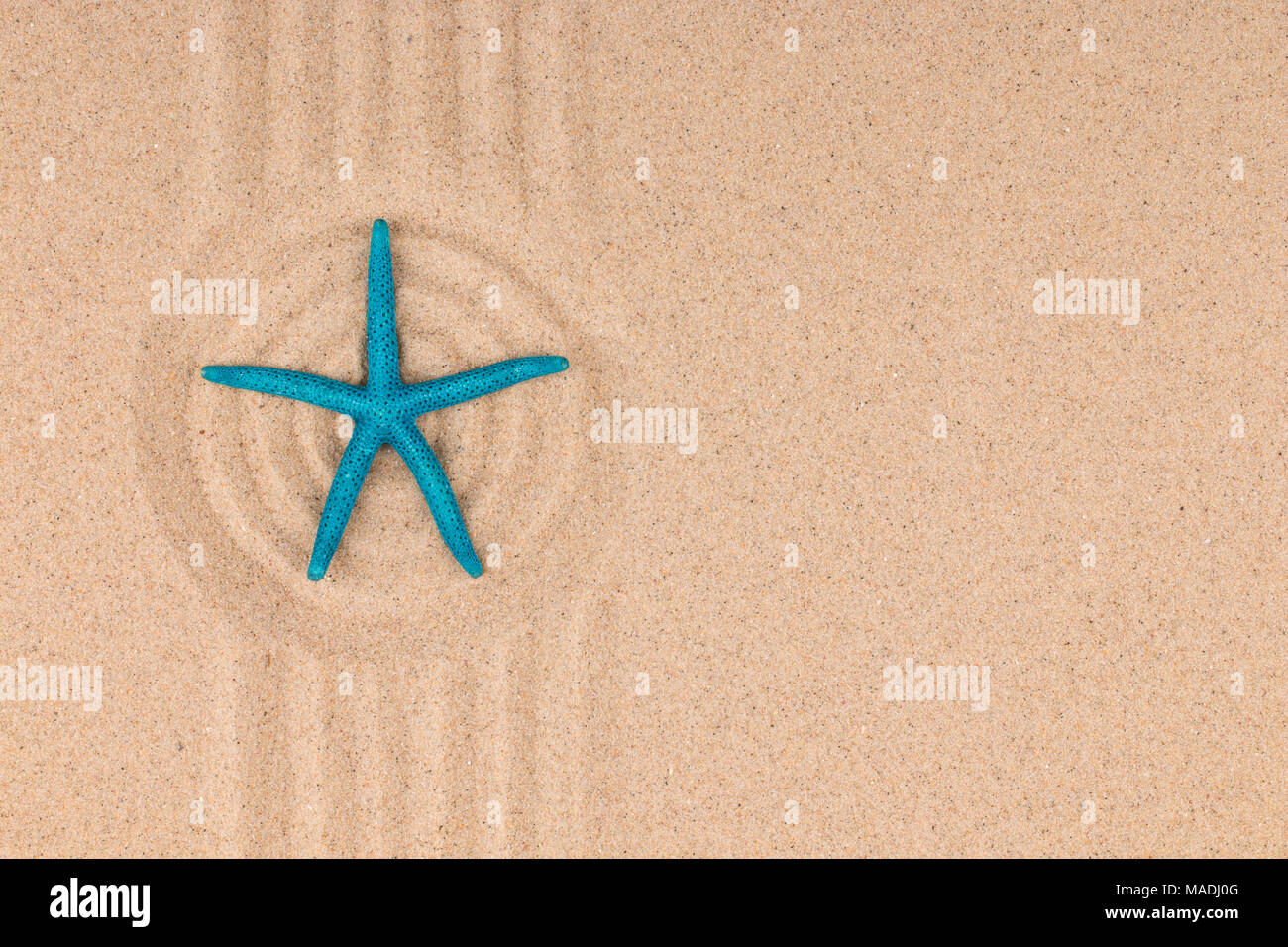 Blue sea star lies in the center of a circle of sand. Summer concept ...