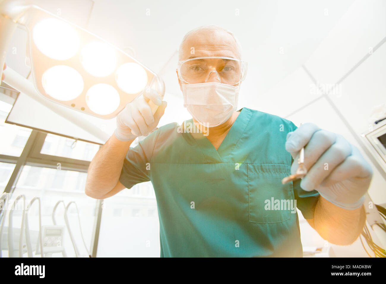 Mature dentist with check-up instrument turning lamp towards patient ...
