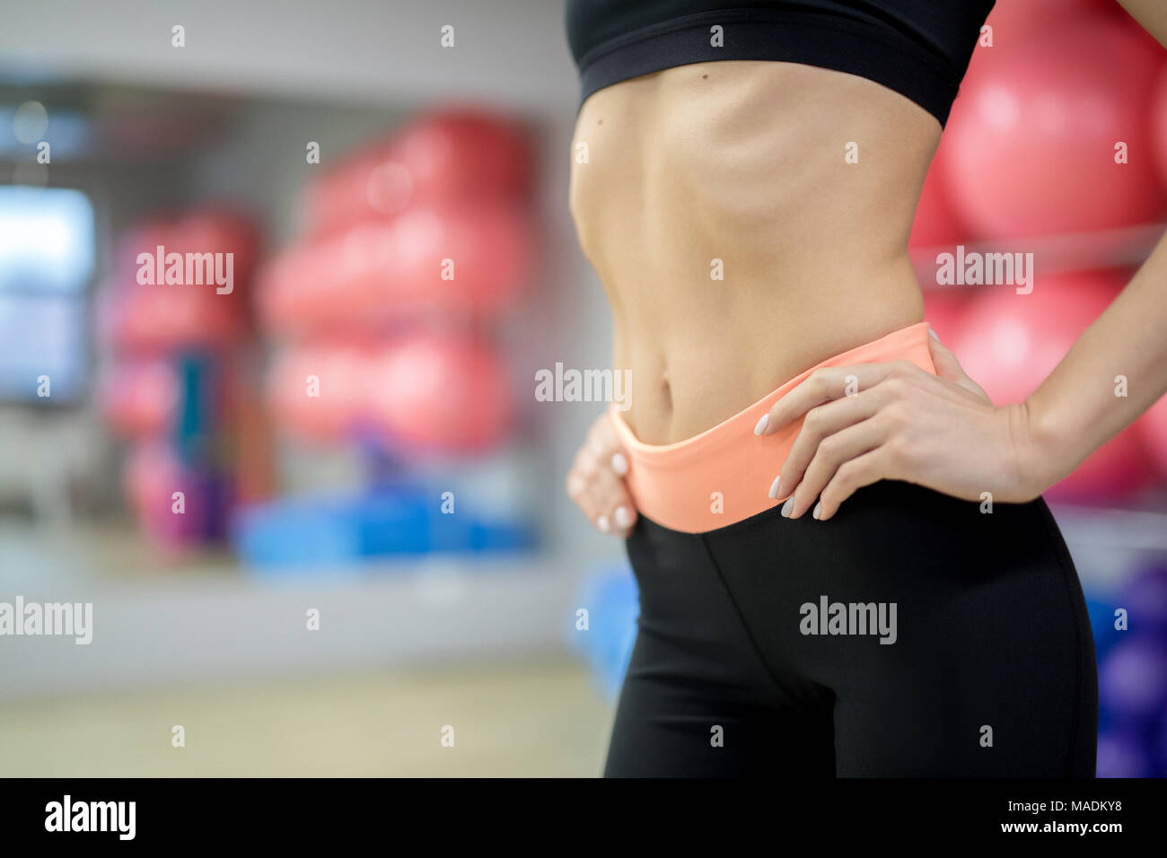 Mid-section of fit and slim girl in activewear keeping her hands on ...