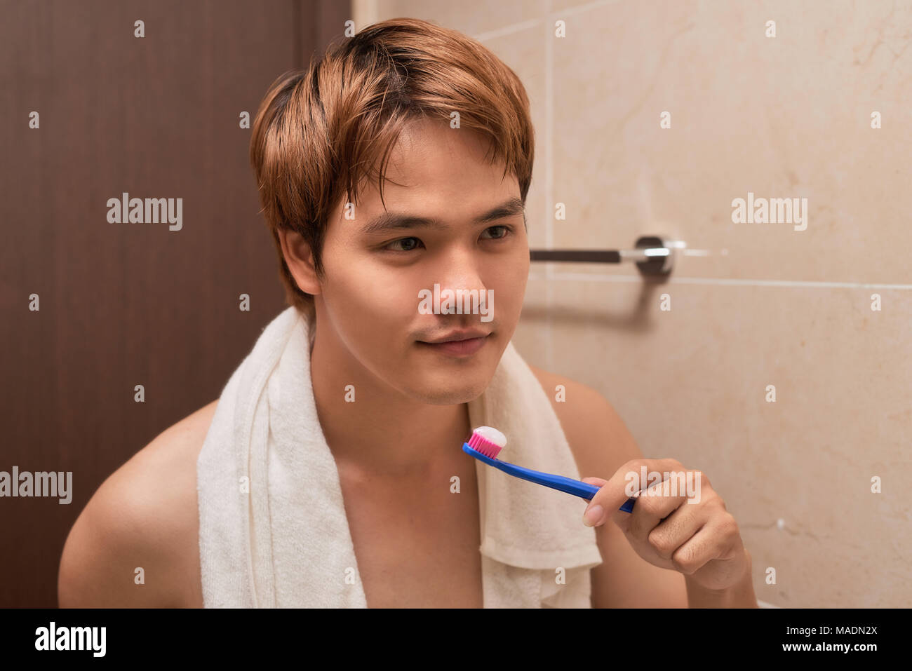 Brushing teeth in the morning. Attractive young man brushing teeth with ...