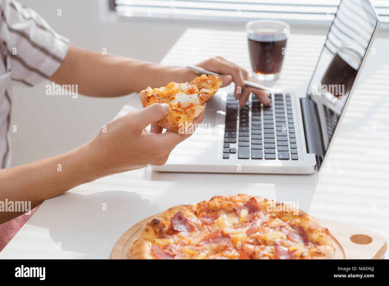 close up man hand eating pizza while working in laptop computer Stock ...