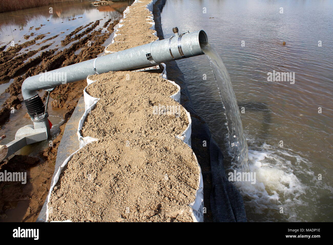 Water pump pumping flood water over tall sandbox barriers through large ...