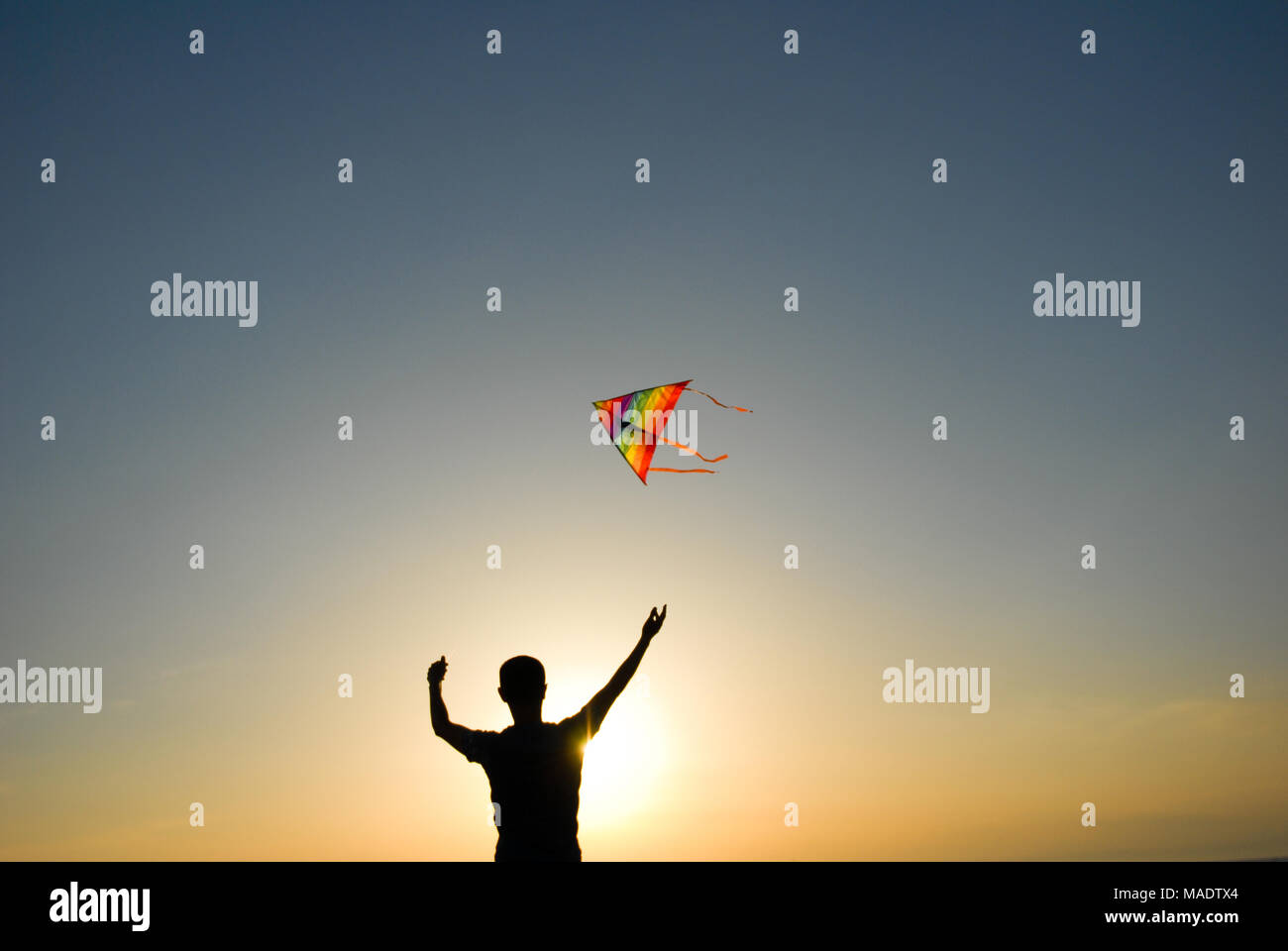 silhouette of active young man controlling colorful kite flying in air ...