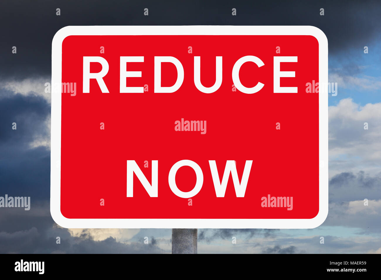 Red and white warning road sign with REDUCE NOW text in front of dark ...