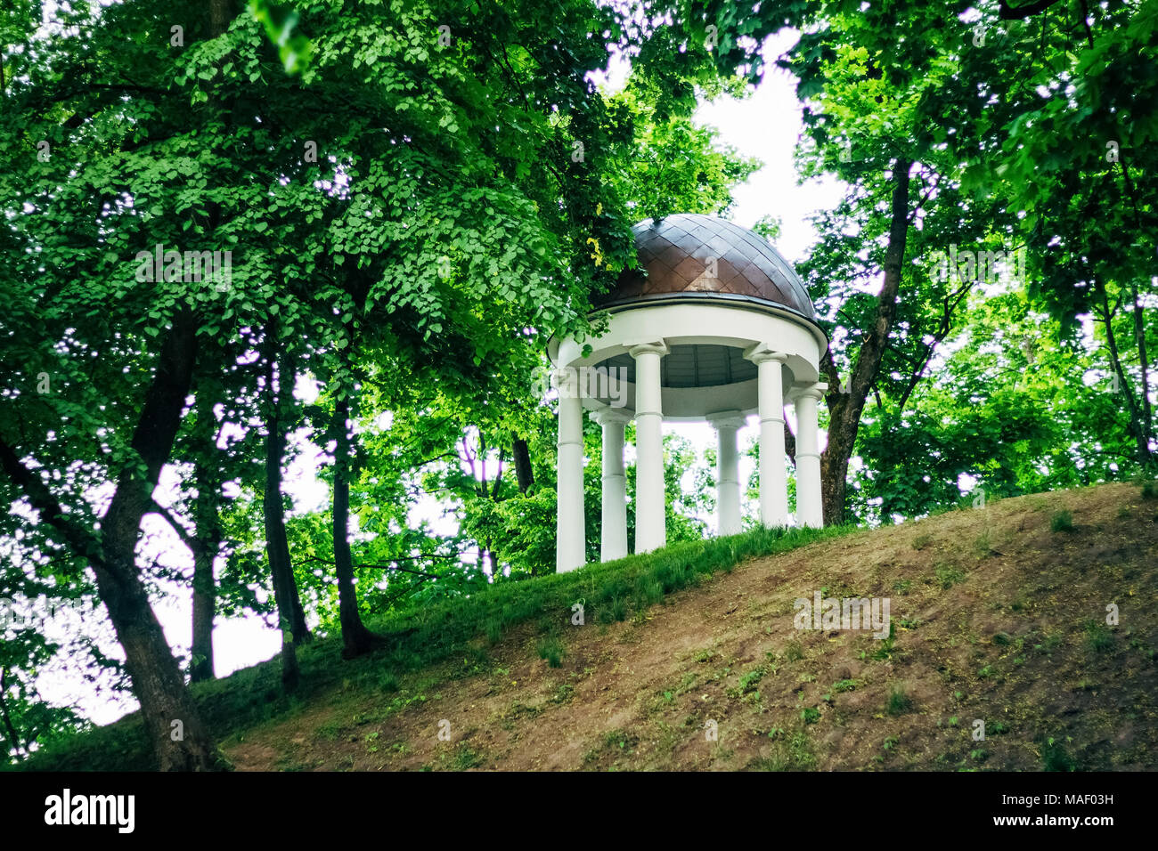 Stone rotunda on a hill in Gomel Park among trees with green foliage ...