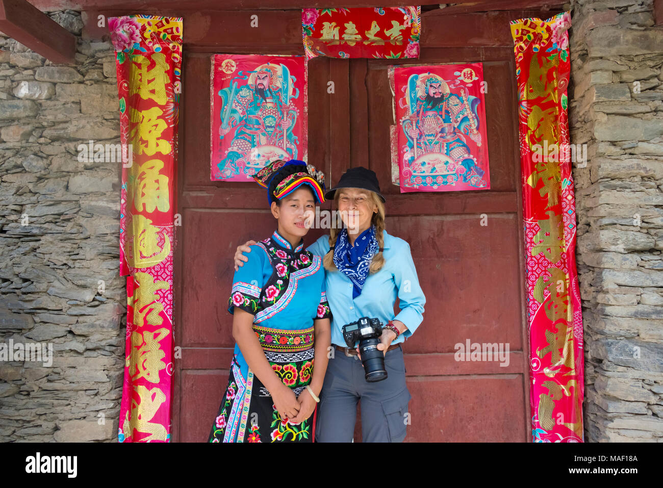 Qiang girl in traditional clothing with western tourist by door of ...