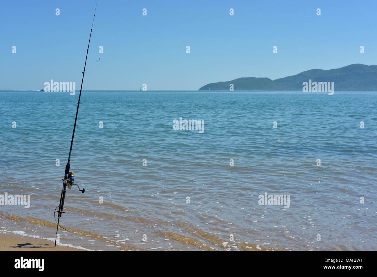 Lone fishing rod on a beach overlooking the ocean and distant mountains ...