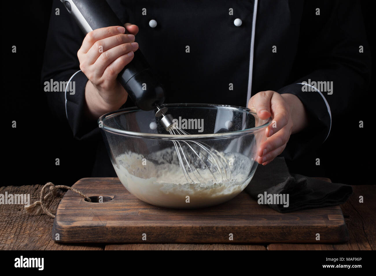 Female chef stirring his batter with a whisk on a black background ...