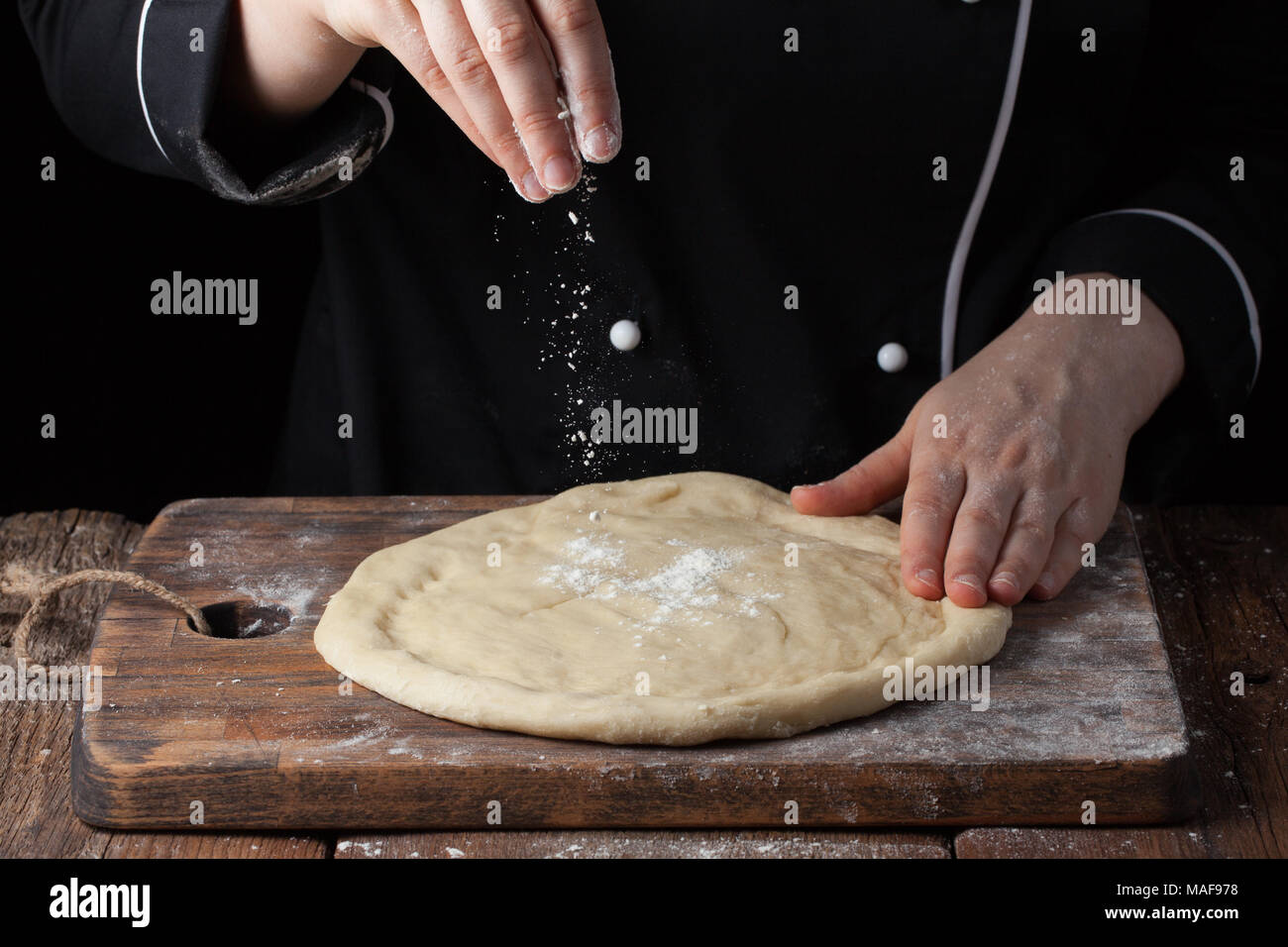 Chef hands pouring flour powder on raw dough using sieve on a black ...