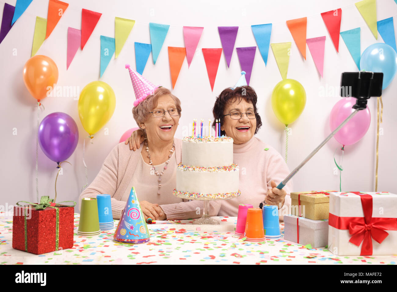 Two cheerful elderly women with party hats and a birthday cake taking a ...