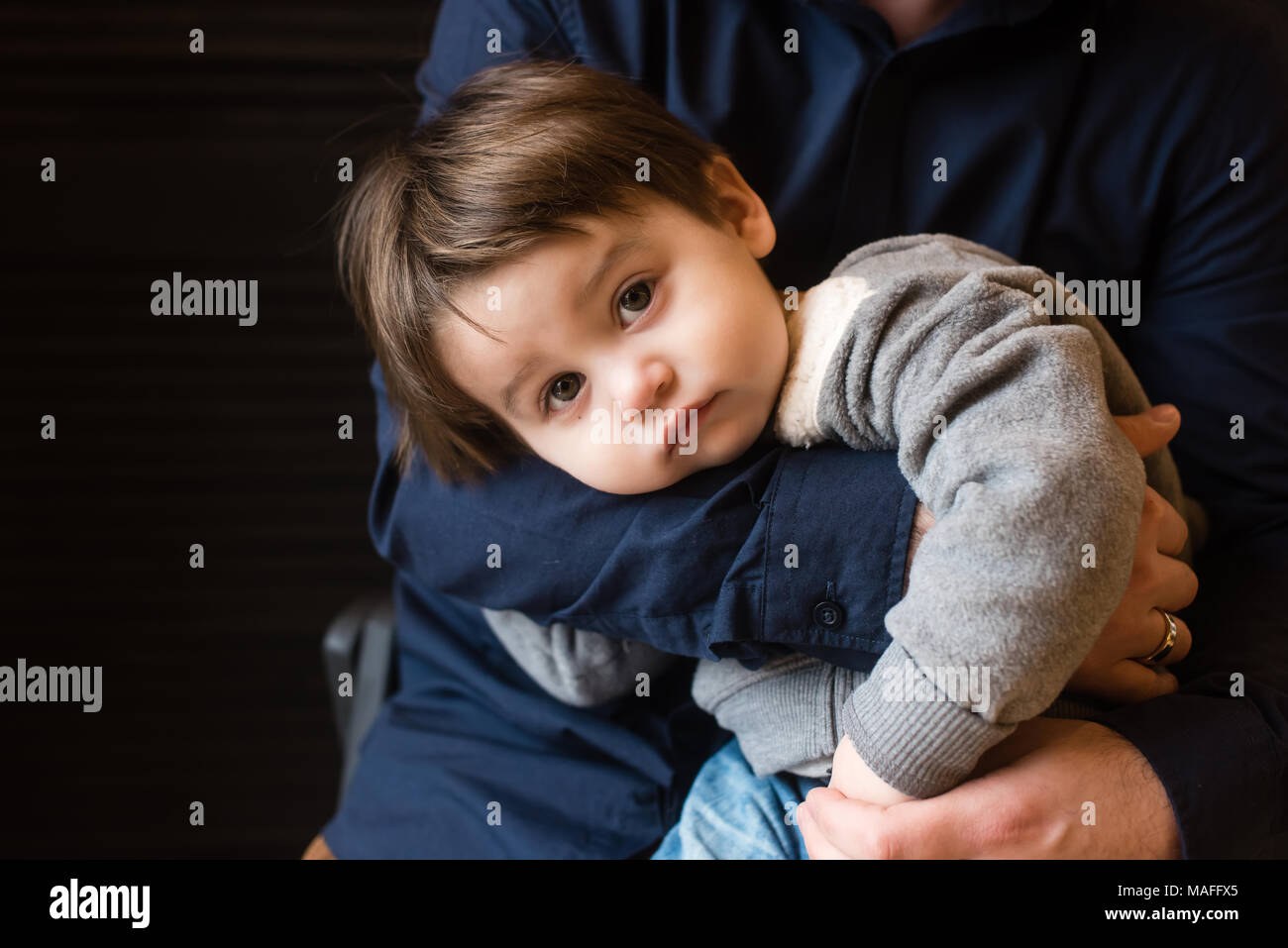 Portrait of small kid in father hugs at black background. Sad child ...