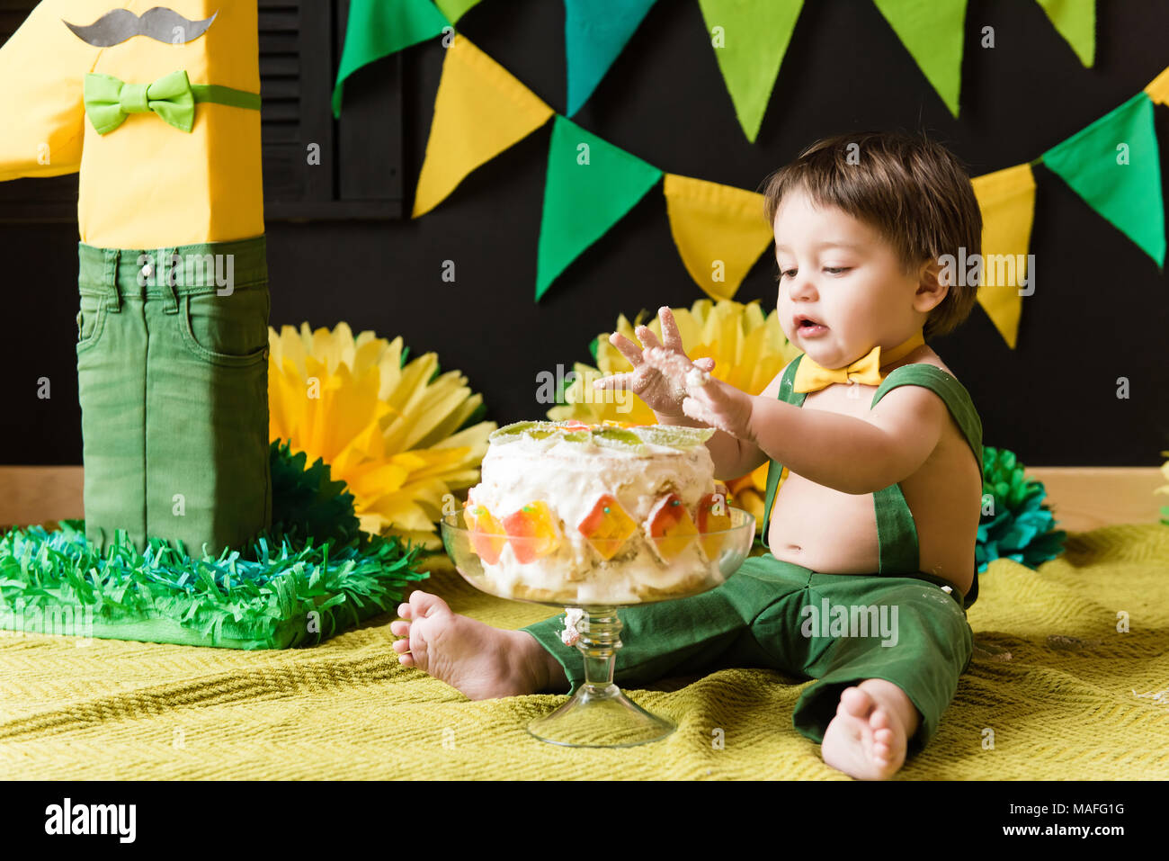 Little baby destroy birthday pie in yellow and green paper decor. First ...