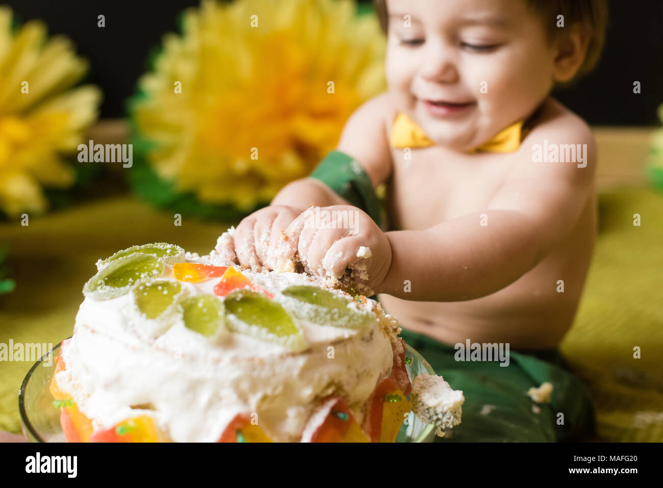 Happy boy destroy sweet pie with cream and fruits at his first birthday ...