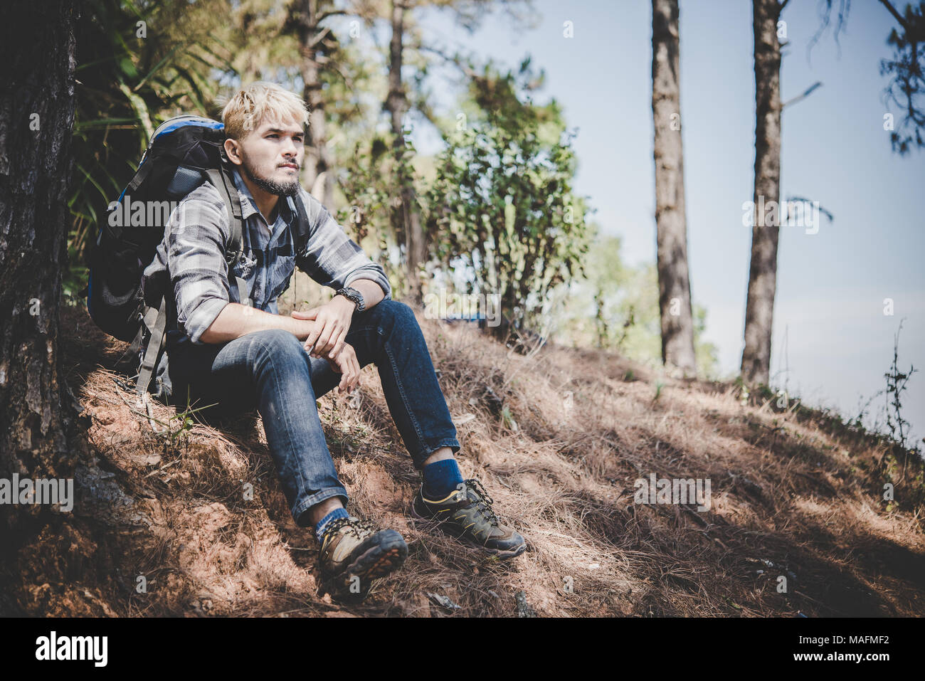Young tired hiker with backpack sitting on the mountain top while ...