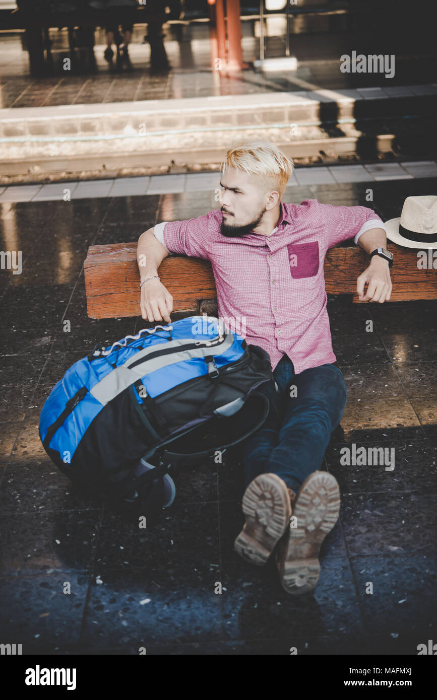 Young hipster man sitting on wooden bench at train station. Man sitting ...