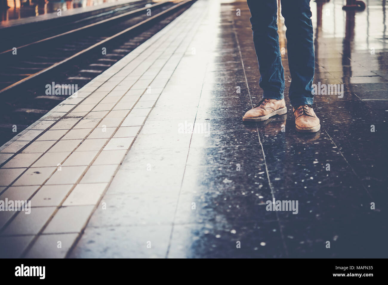 Feet of a young man wearing jeans who is waiting for the train at the ...