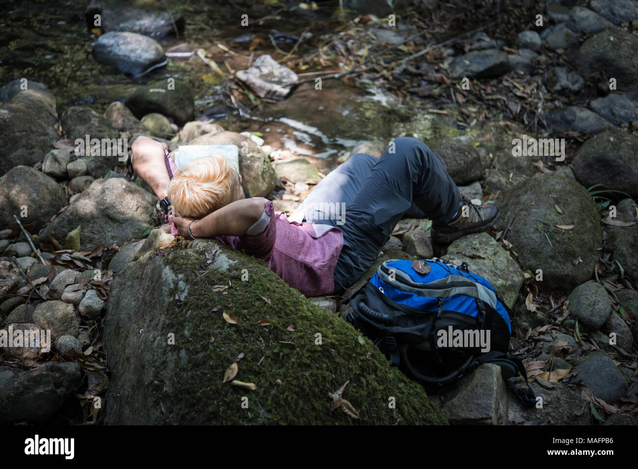 Young tired hiker with backpack sitting on the rock in forest while ...