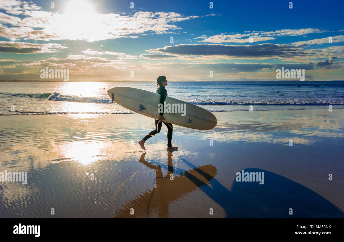 Surfer carrying a longboard on the beach at The Pass, Byron Bay, New ...