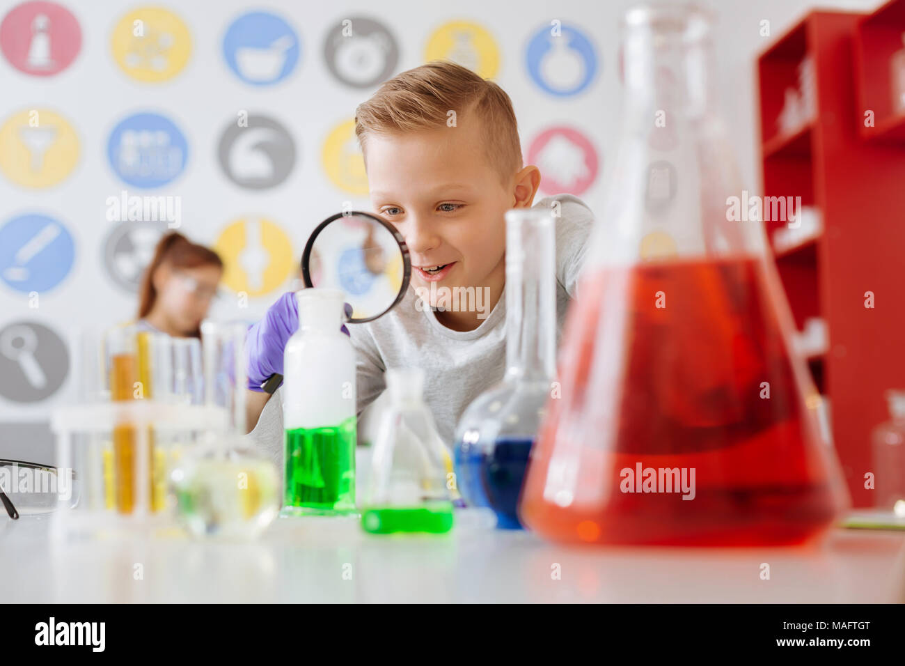 Cheerful student using magnifying glass to study chemical reaction ...
