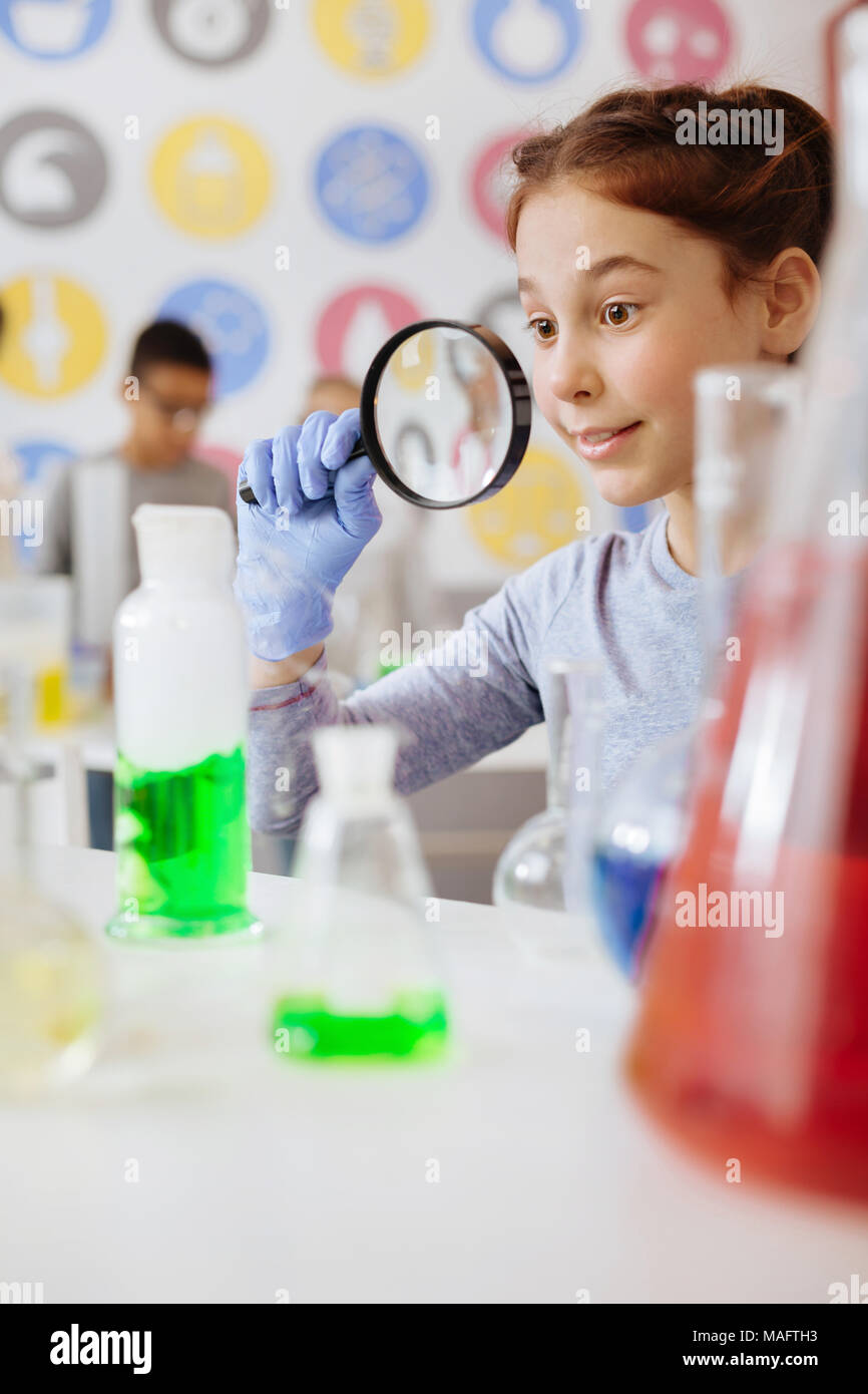 Cute schoolgirl observing chemical reaction through magnifying glass ...