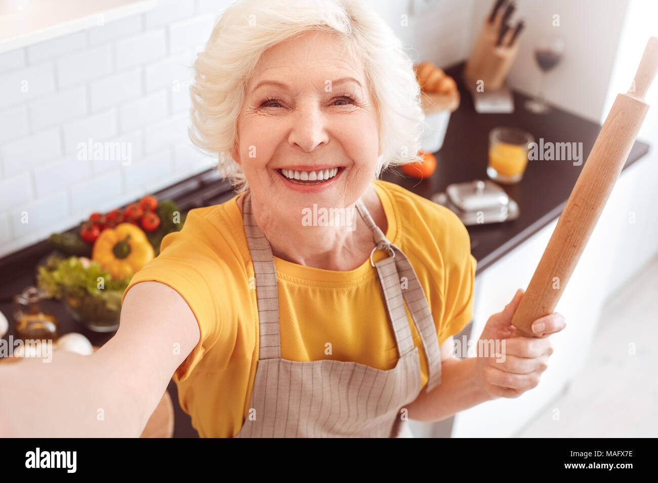 Old housekeeper making selfie toothy smile, holding a rolling pin ...