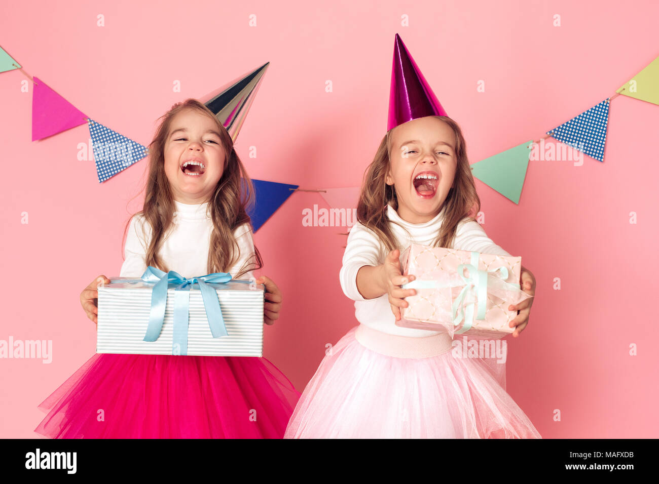 Two little children girls celebrating birthday studio isolated on pink ...