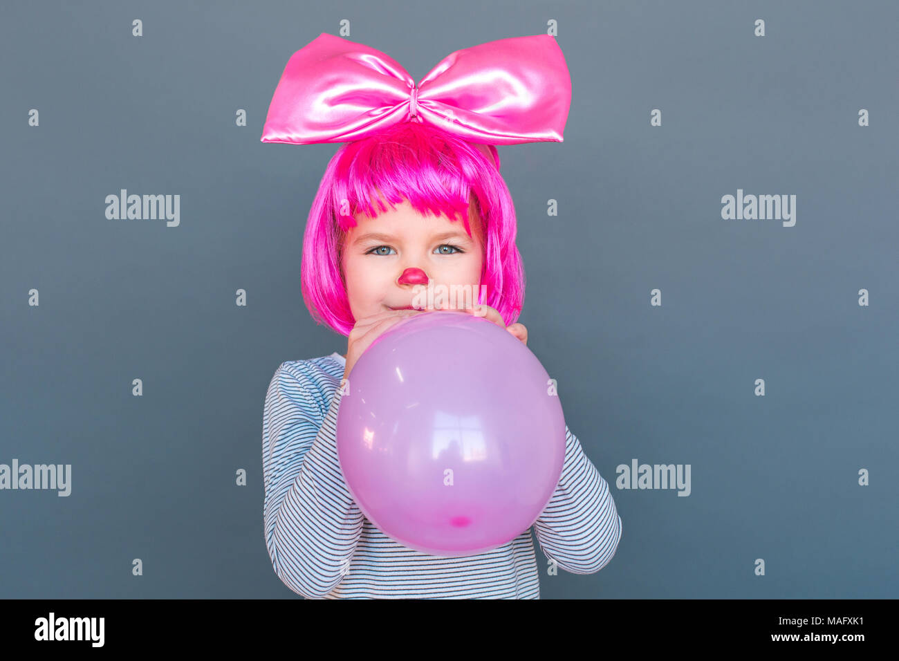 Portrait of cute little girl wearing pink wig, inflates balloon. Studio ...