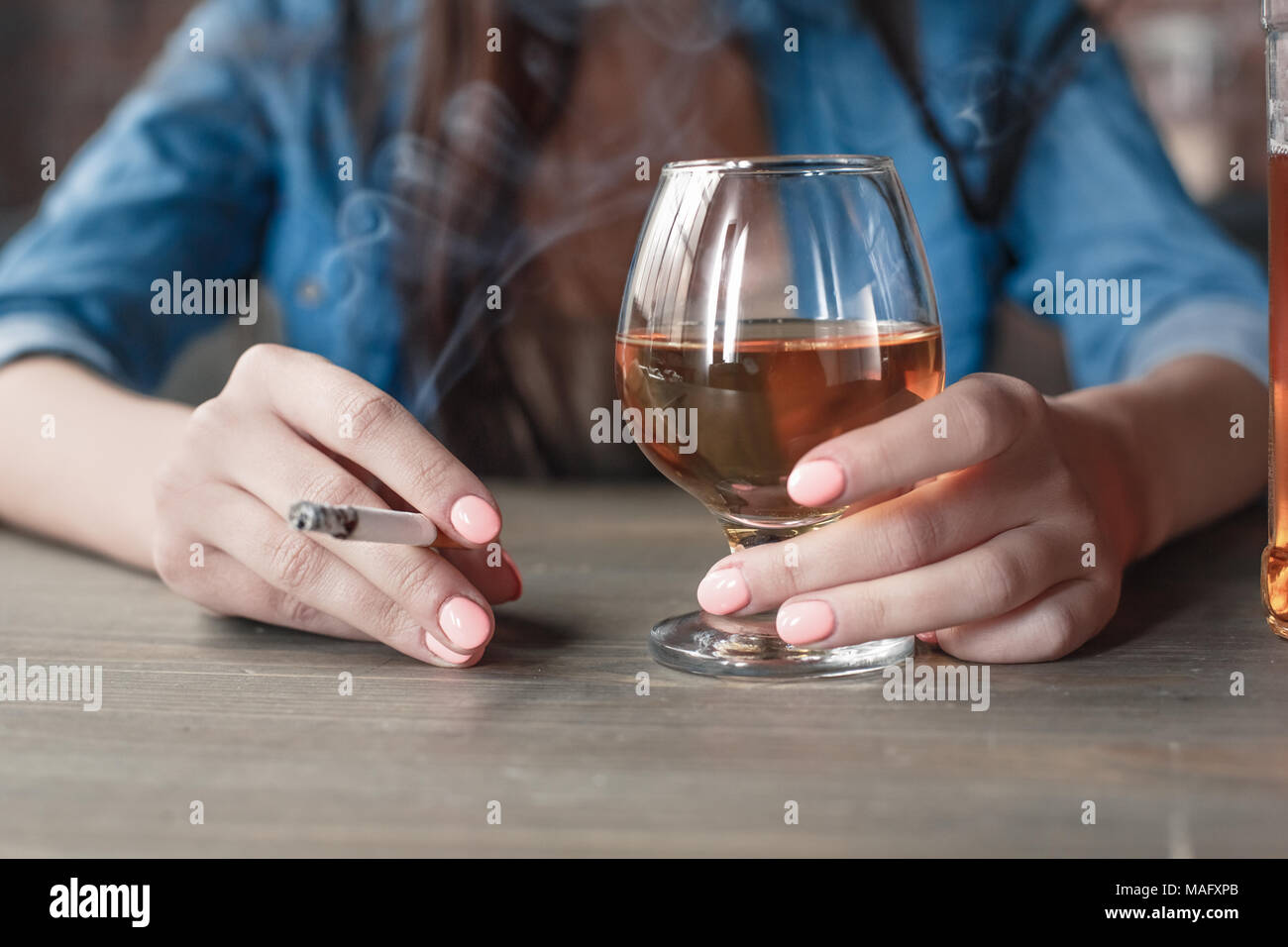 Young female alcoholic smoker social problems sitting at table holding ...