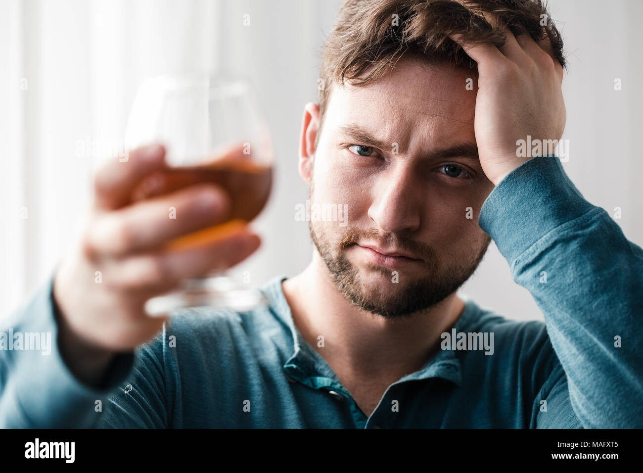 Young man at living room alcohol problems holding glass of whiskey ...