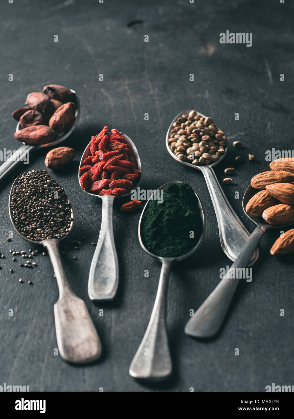 Spoons of various superfoods on black wooden table background ...