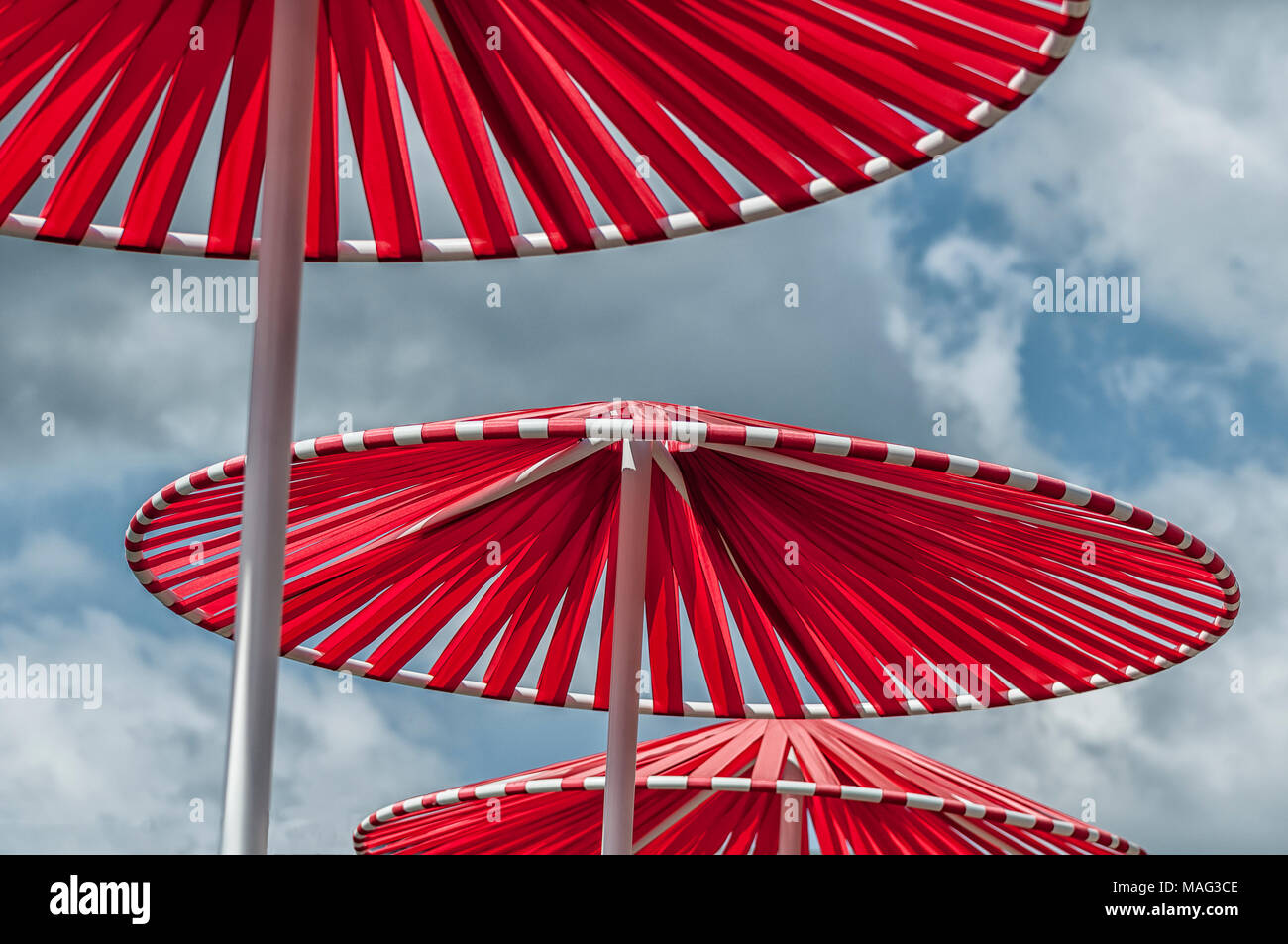 three red parasols against a blue cloudy sky Stock Photo - Alamy