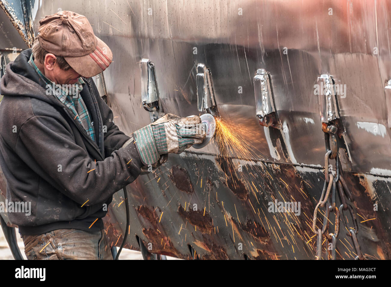 a metal worker is grinding the wall of a ship with a grinder Stock ...