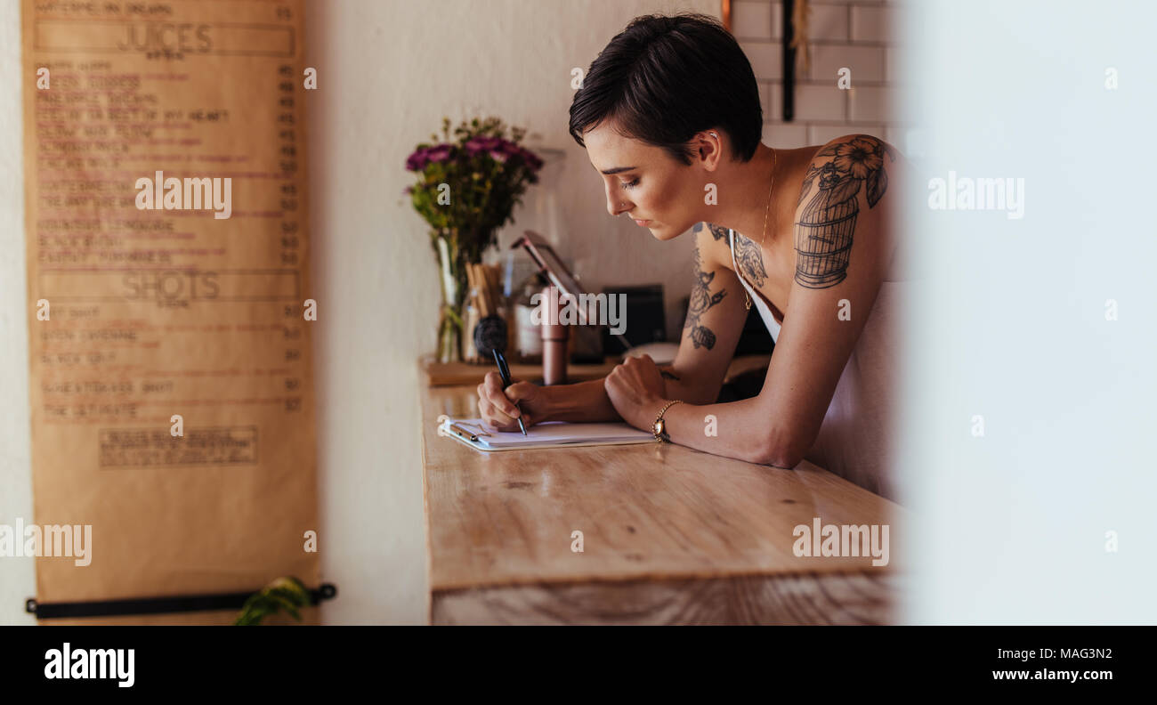 Woman standing at the counter of her cafe noting orders. Restaurant ...