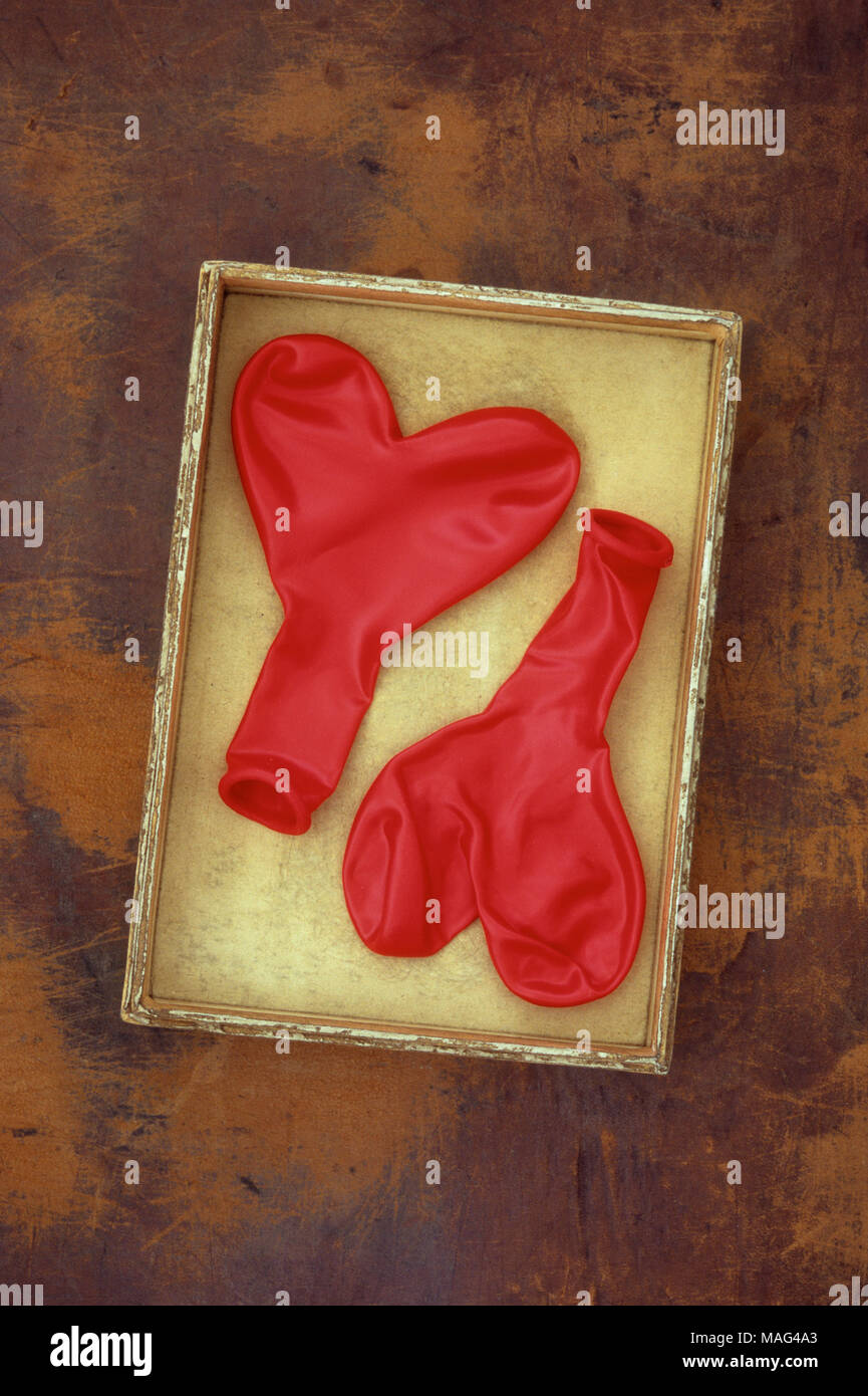 Two flat red party balloons which inflate to give heart shape lying in ...