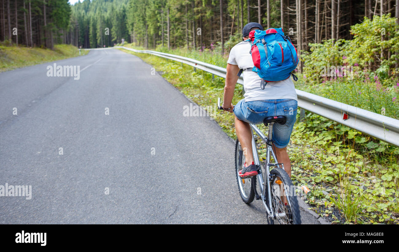 Young man with backpack cycling on road in mountains. Bicycle tourism ...