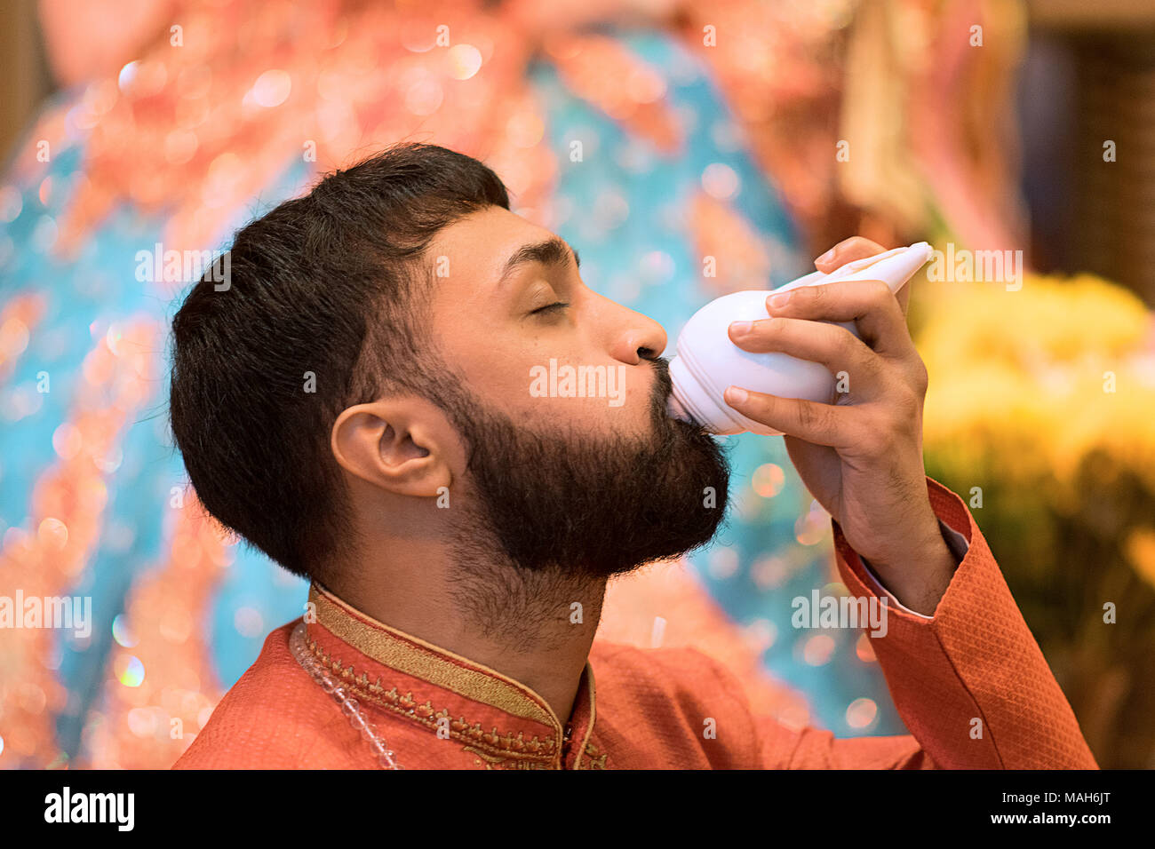 A young man blows into a large white conch shell during morning ...