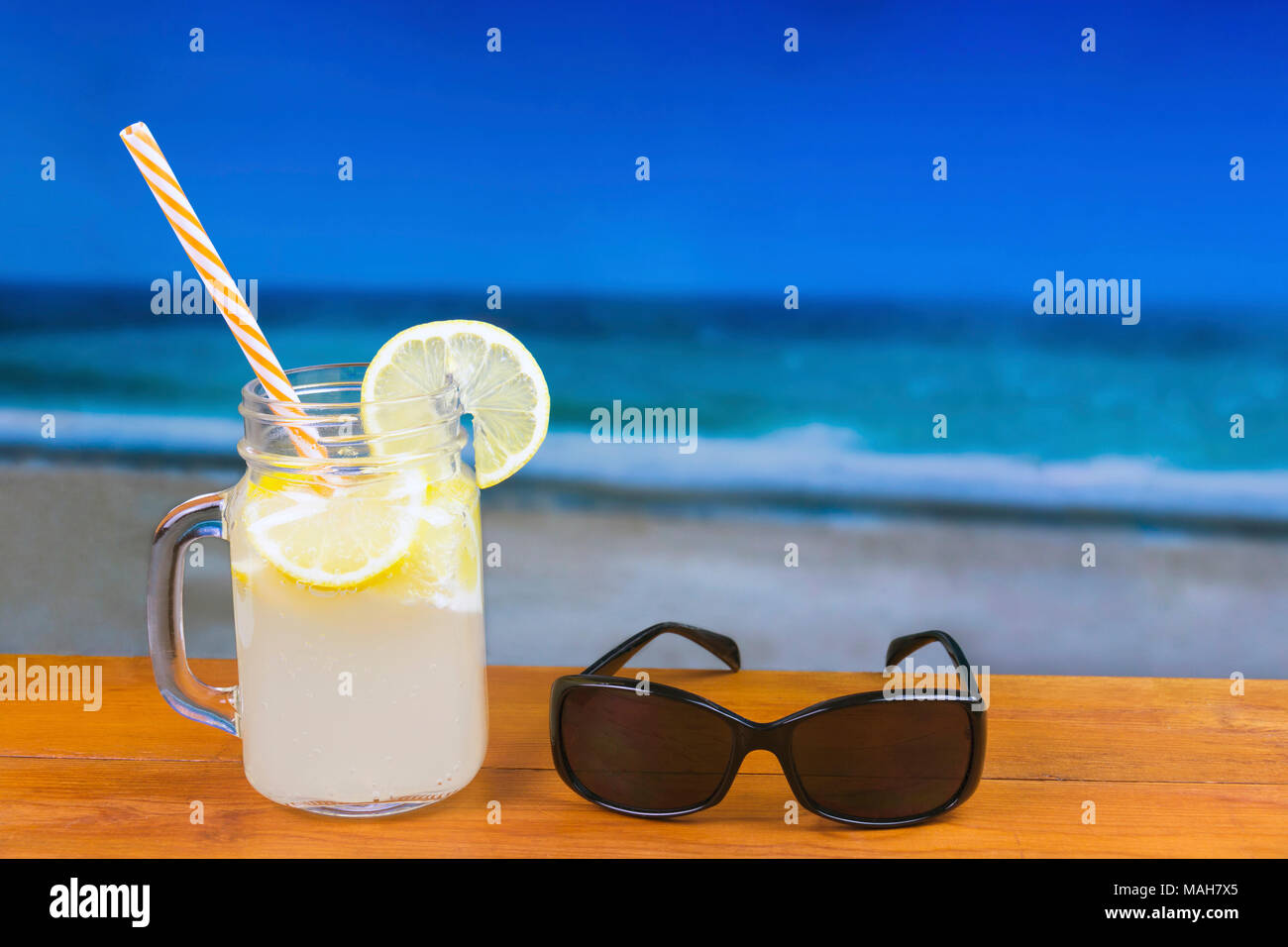 Refreshing lemon drink on a wooden table with sunglasses against a out ...