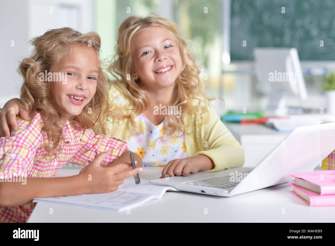 Two girls at class using laptop and writing Stock Photo - Alamy