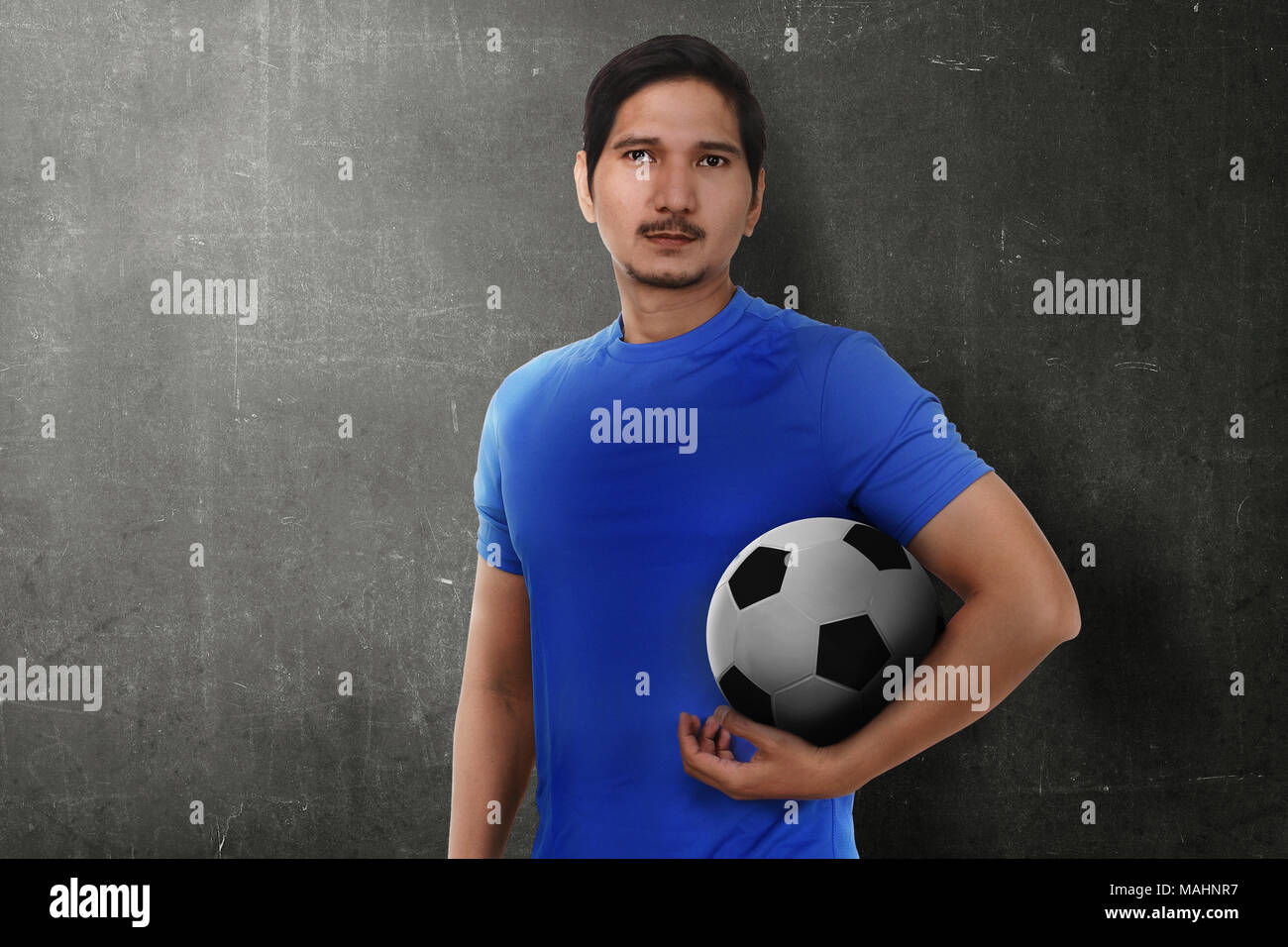 Attractive asian soccer player holding the ball over dark wall ...