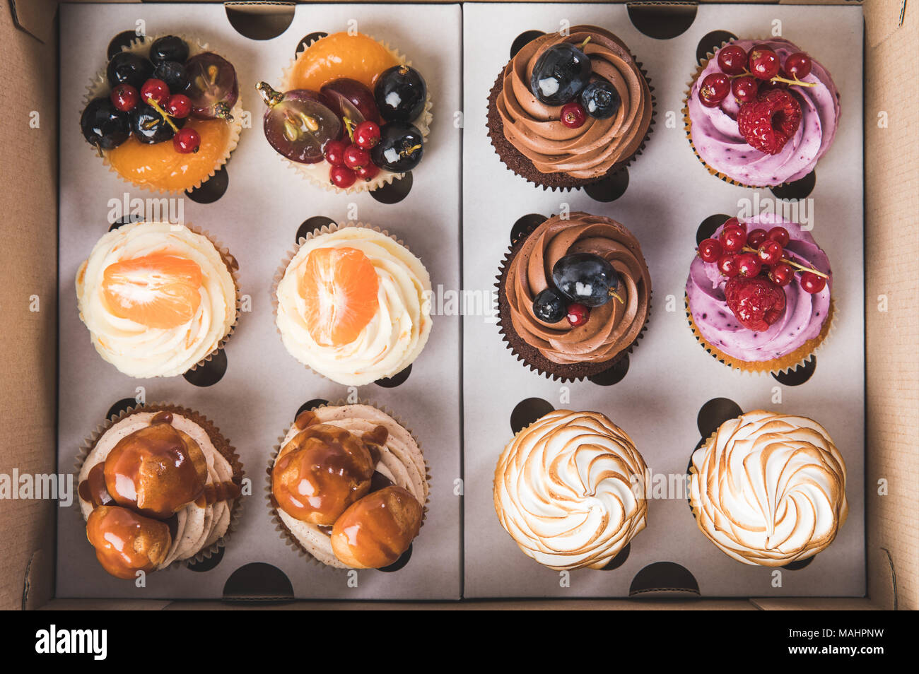 close up view of various types of cupcakes in cardboard box isolated on ...